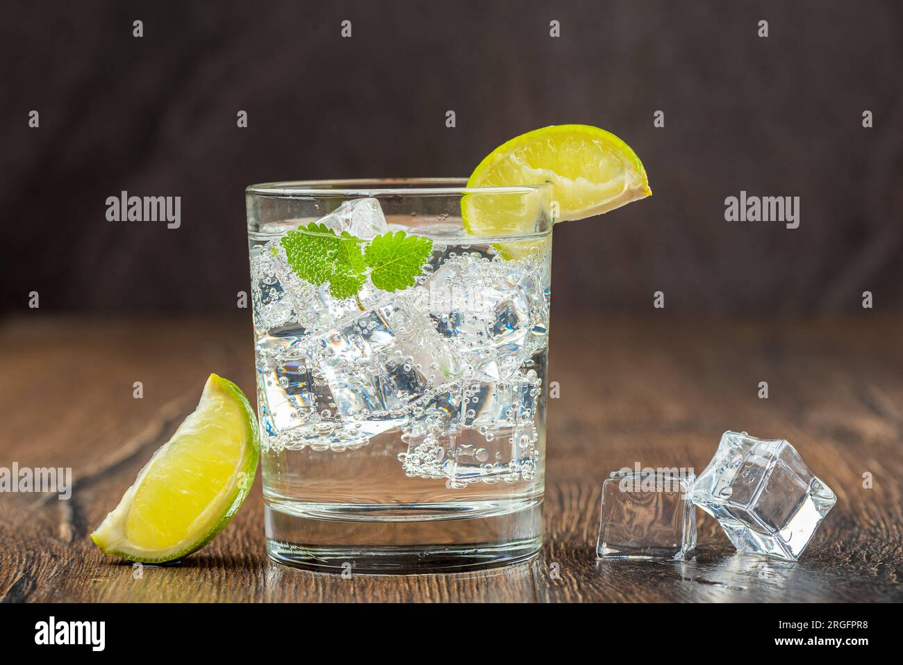 A glass of refreshing mineral water with ice cubes, mint leaves and lime slices on a wooden bar ...