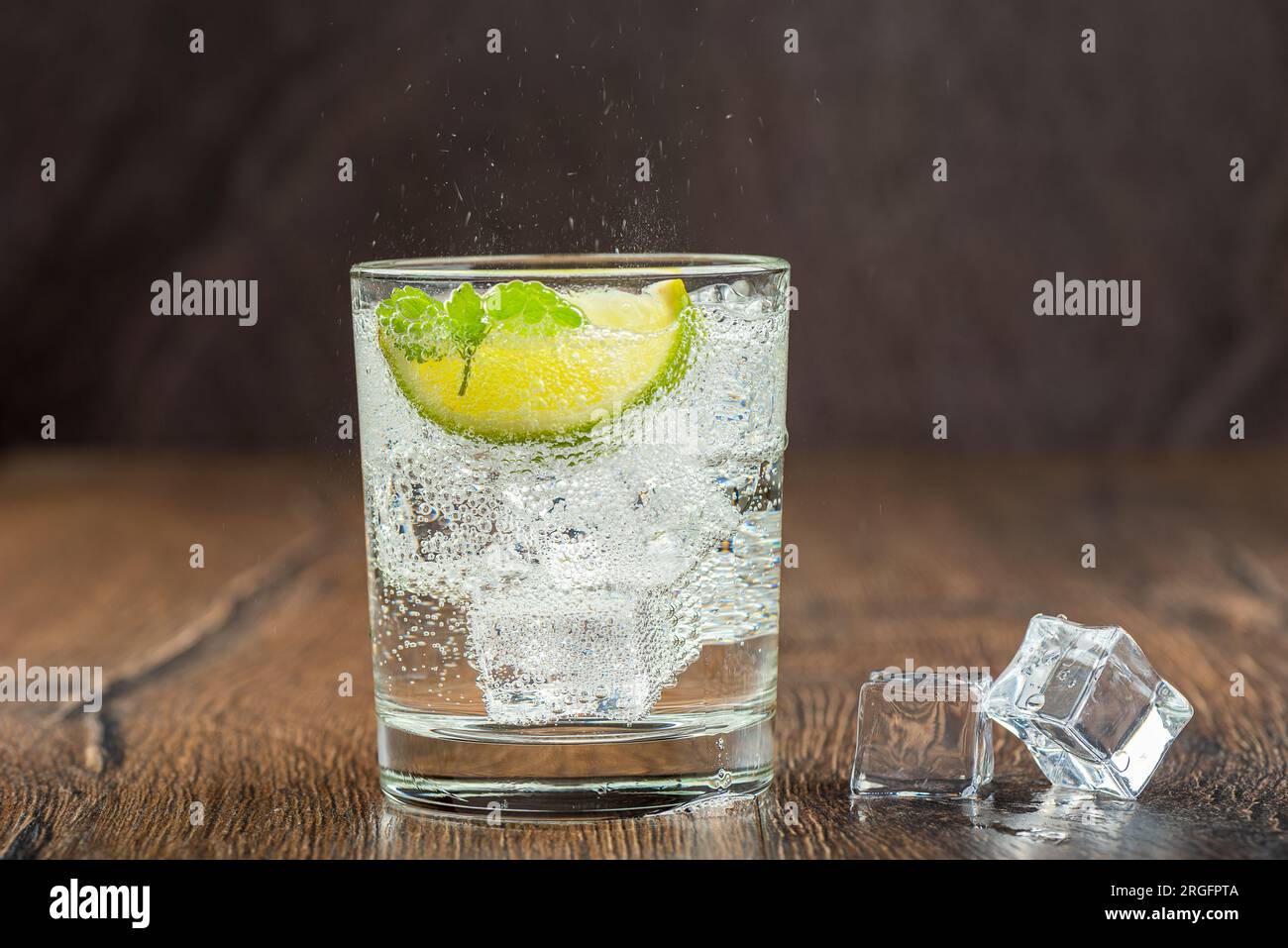 Refreshing mineral water in a glass with ice cubes, mint leaves and lime slice. Spray over a ...