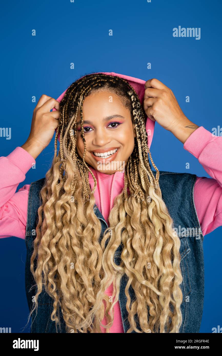 positive dark skinned woman wearing pink hood on head, looking at ...