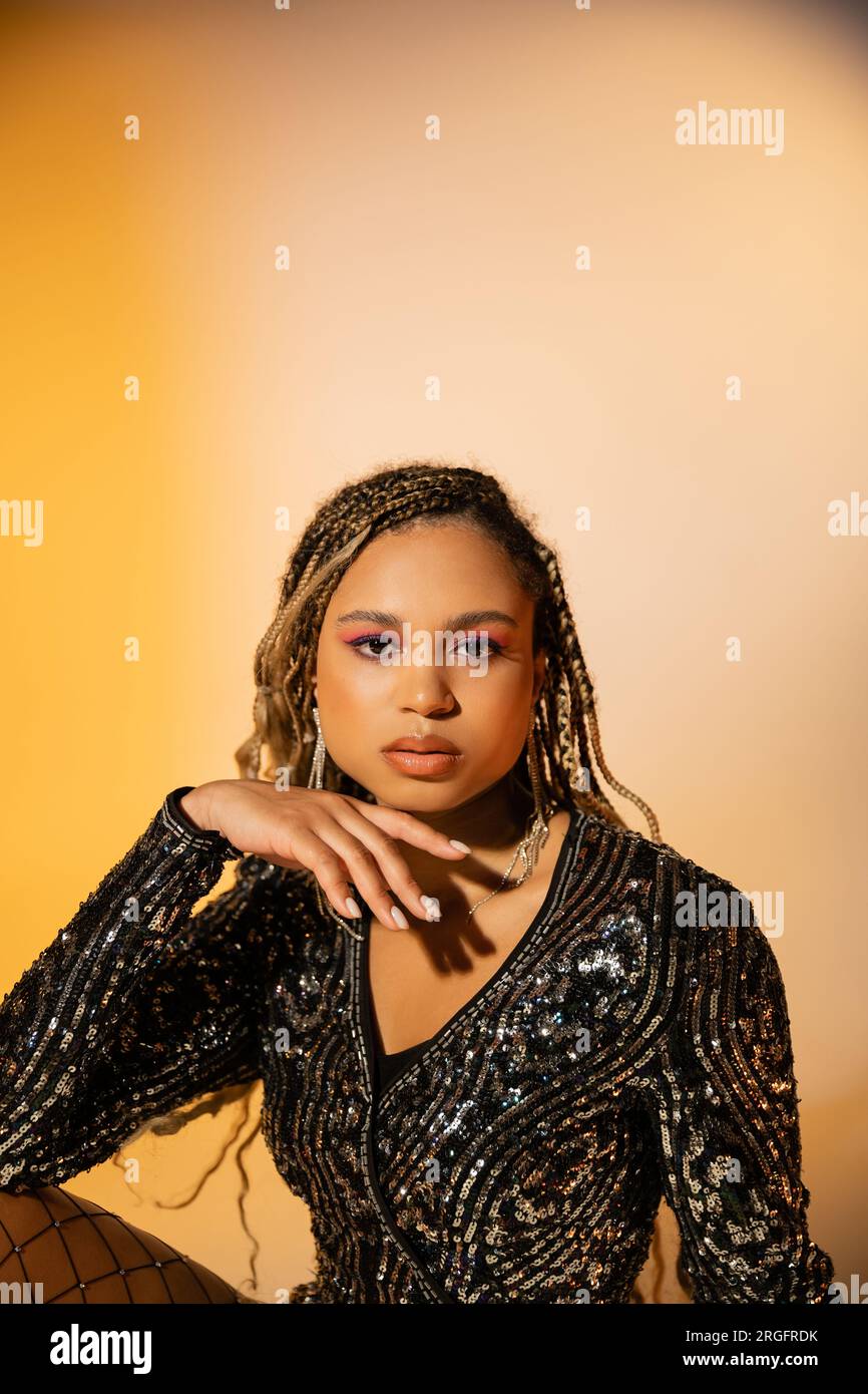 beautiful woman in party outfit looking at camera on yellow background ...
