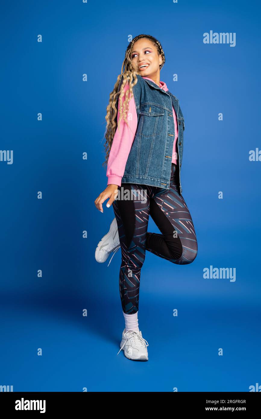 full length, dark skinned woman in sporty outfit posing on blue ...
