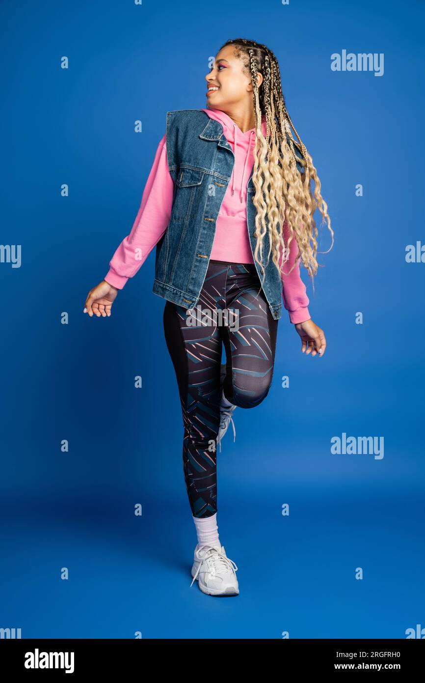 full length, dark skinned woman in sporty outfit smiling on blue ...