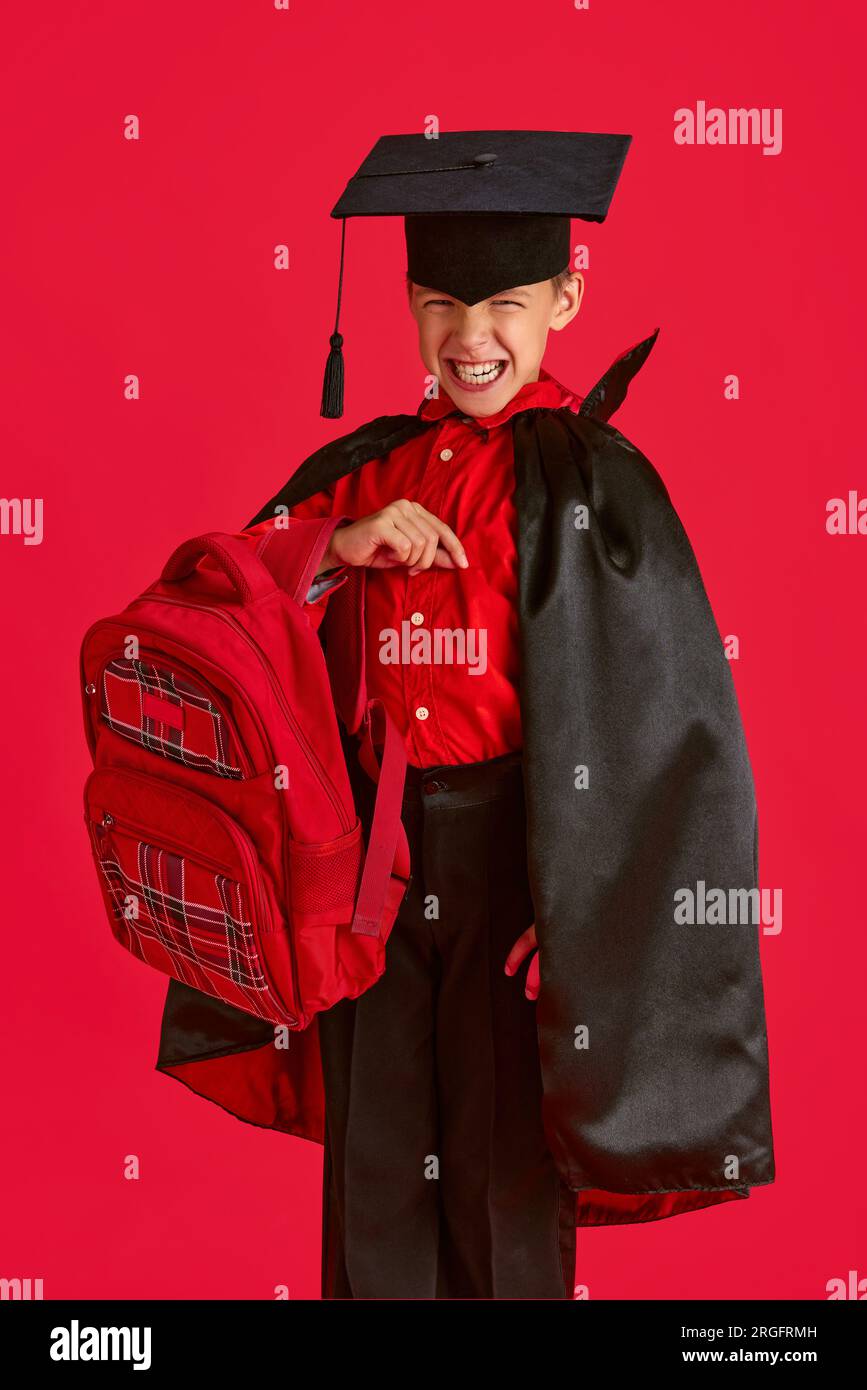 Little boy with grimacing face in graduation hat and mantle standing ...