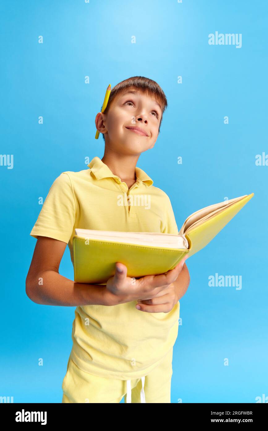 Emotive school boyholding book with dreamy and positive face against ...
