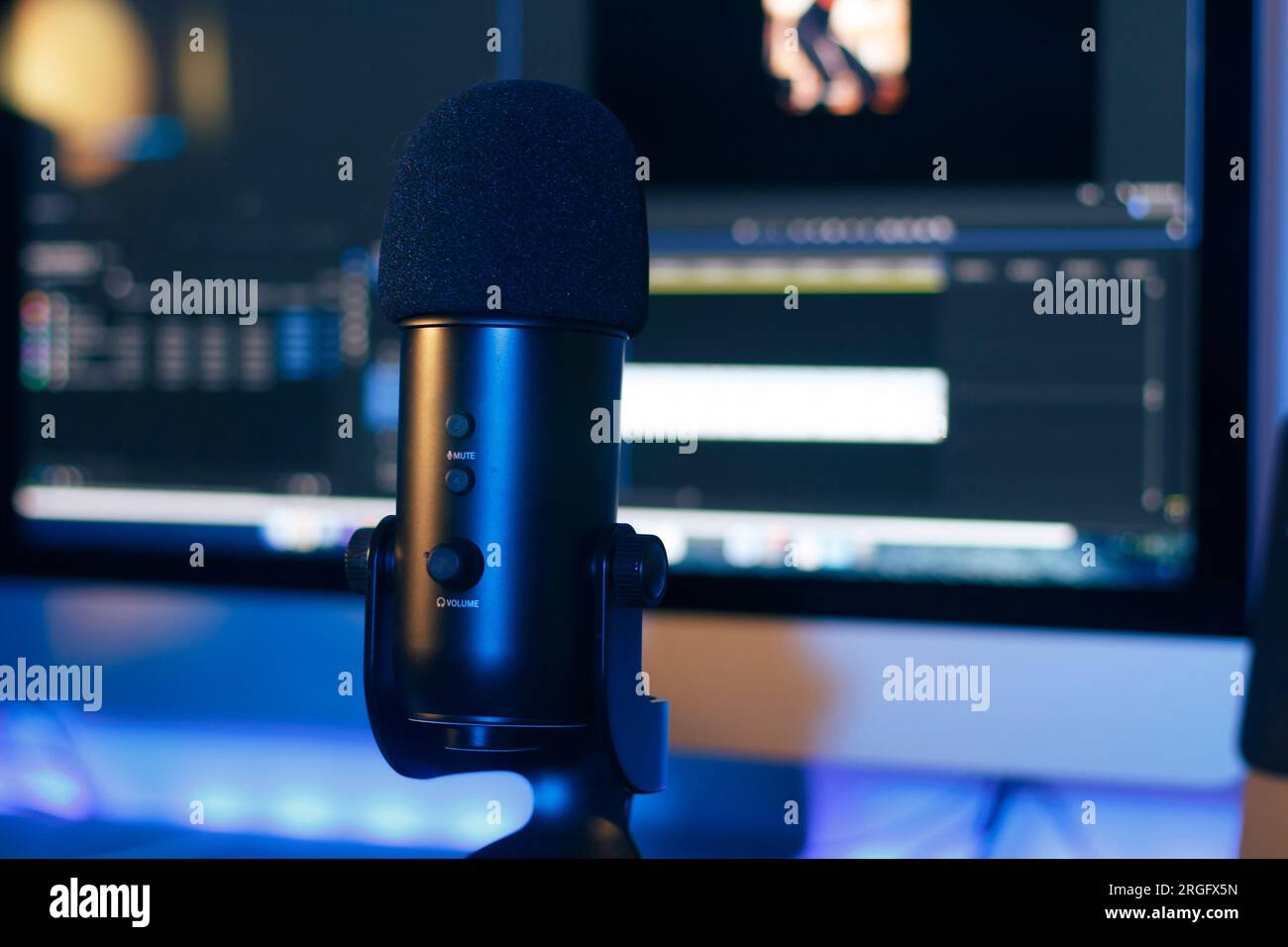 Videomaker desk, close up on a microphone with a blurred monitor in the ...