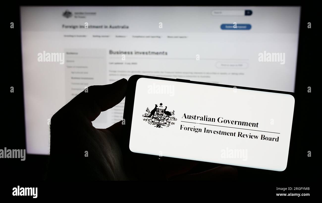 Person holding mobile phone with logo of Australian Foreign Investment ...
