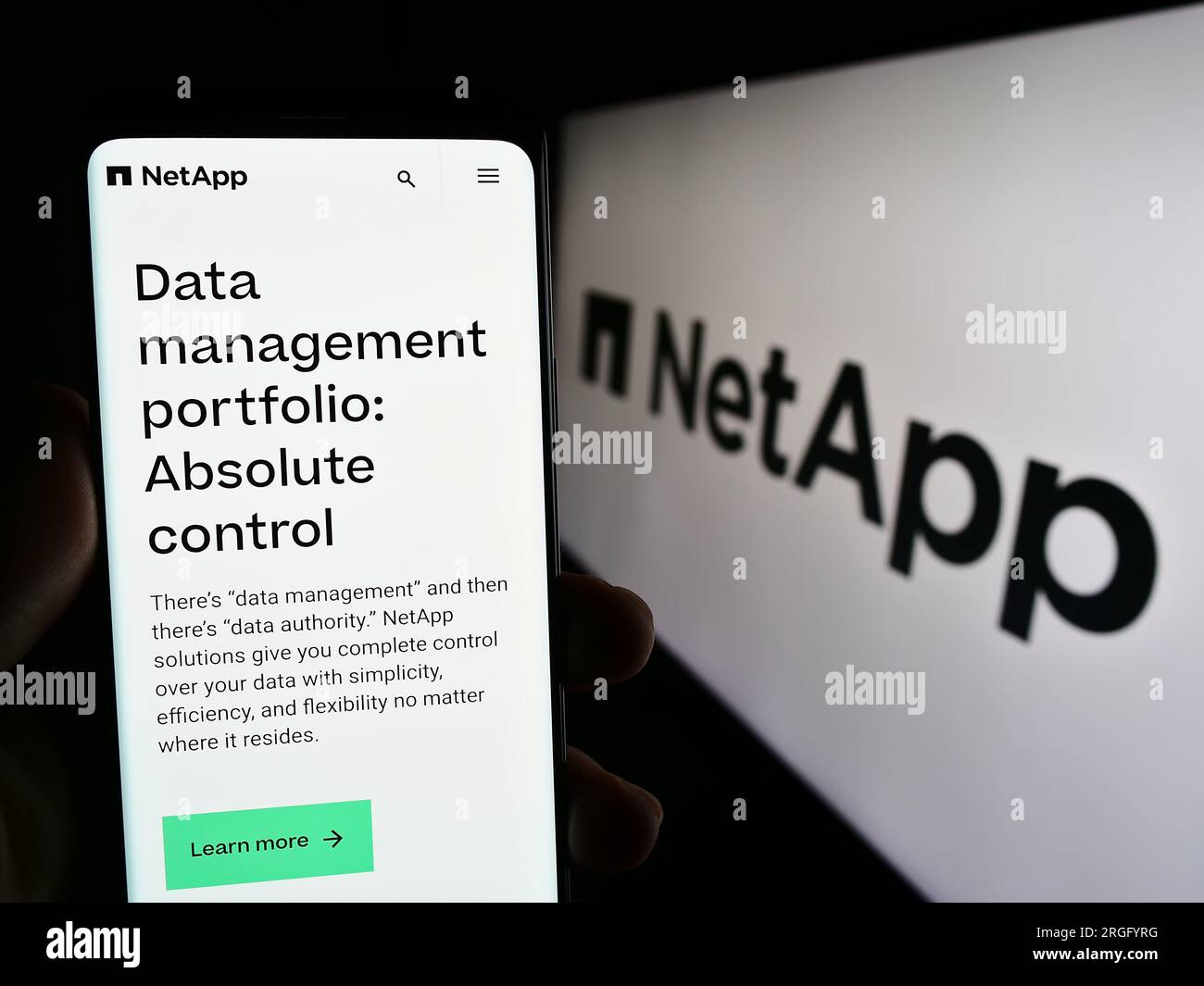 Person holding mobile phone with web page of US cloud company NetApp Inc. on screen in front of ...