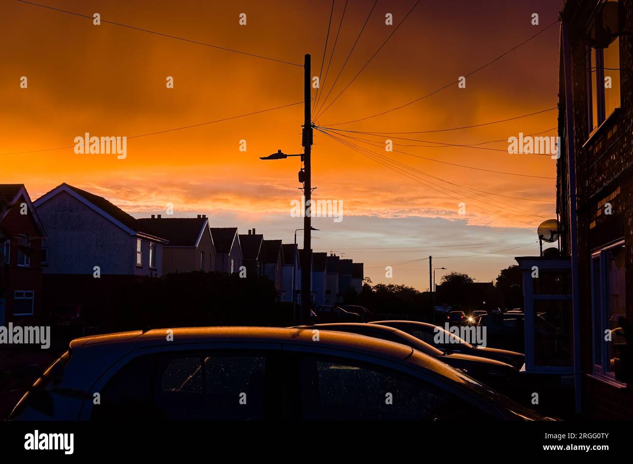 A dramatic orange sky over car roofs on a suburban street at sundown ...