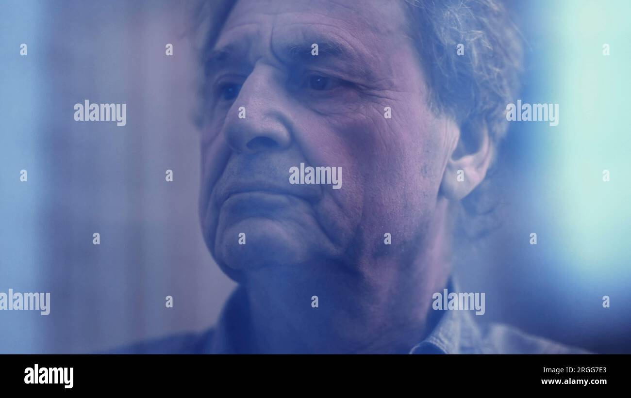 Brooding senior man lost in thought, gazing through his window as the ...