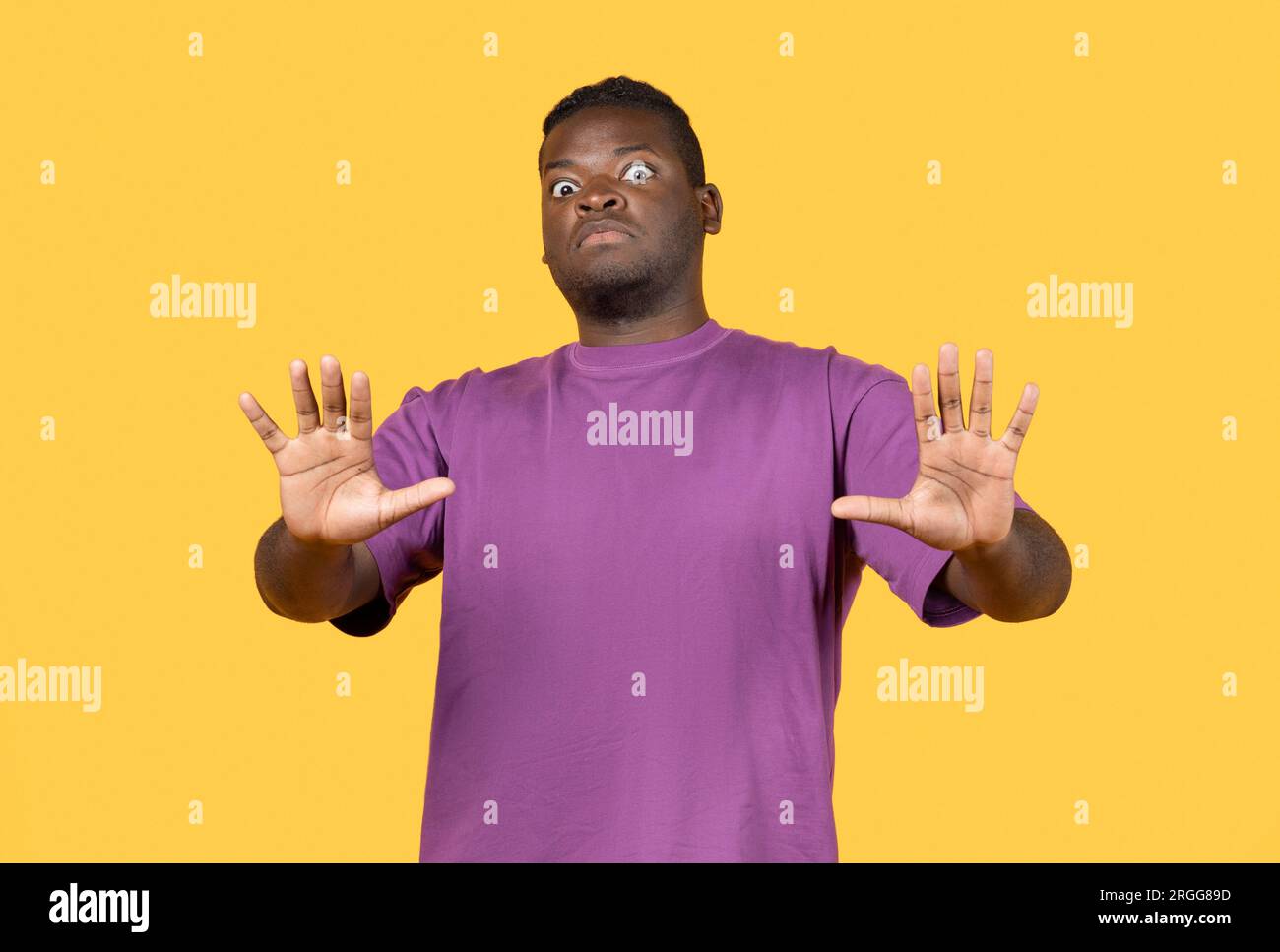 African man making stop gesture pushing camera back, yellow background ...