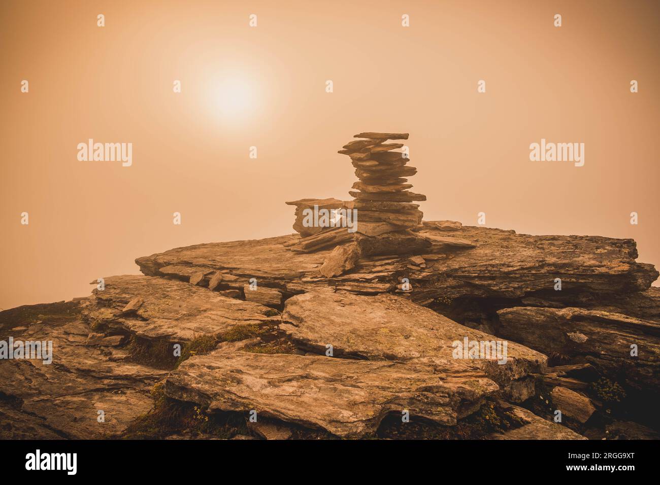 Stacked rocks in the mountains with a sunset in the background and fog ...