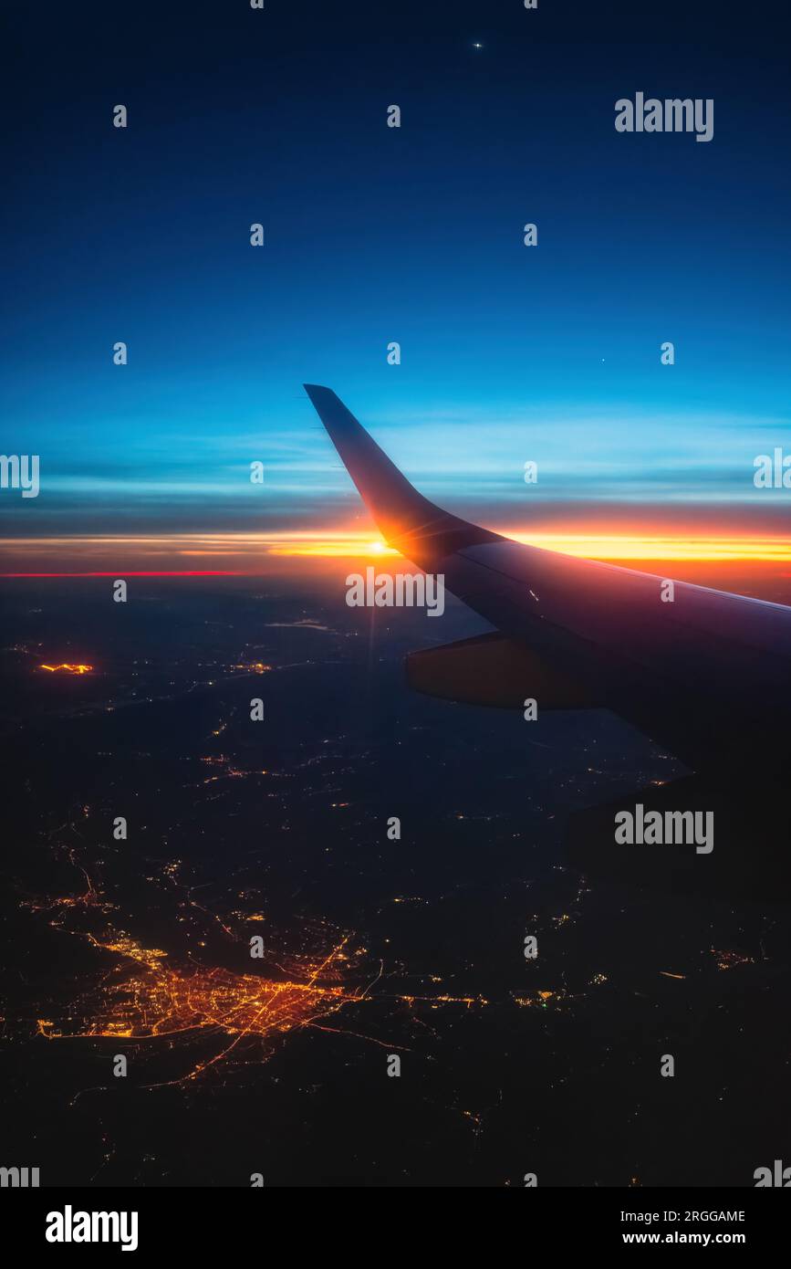 Airplane flight in sunset sky over earth of city light and wing of ...