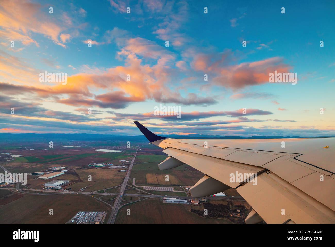 Airplane flight in sunset sky over city and wing of plane. View from ...