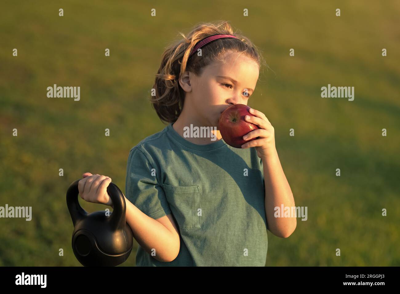 Sporty kid with apple and kettlebell outdoor in summer park. Kids ...