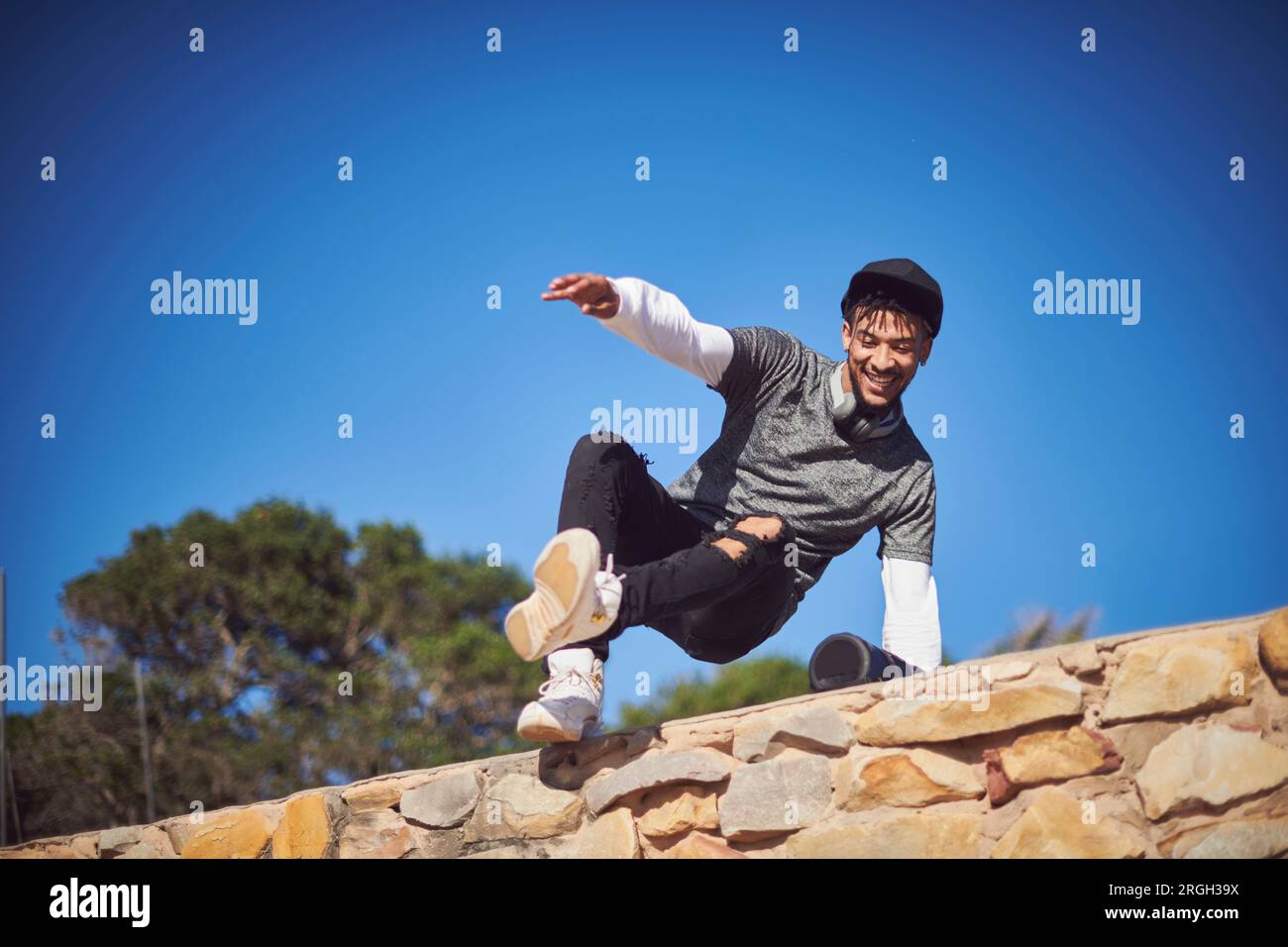 Smiling young man jumping stone wall Stock Photo - Alamy