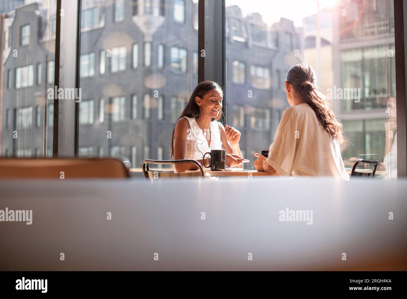 Businesswomen talking at table by window Stock Photo - Alamy