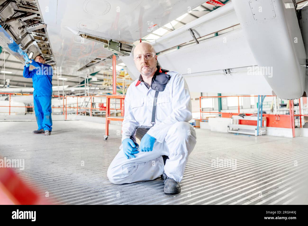 Man holding digital tablet crouched underneath airplane Stock Photo - Alamy