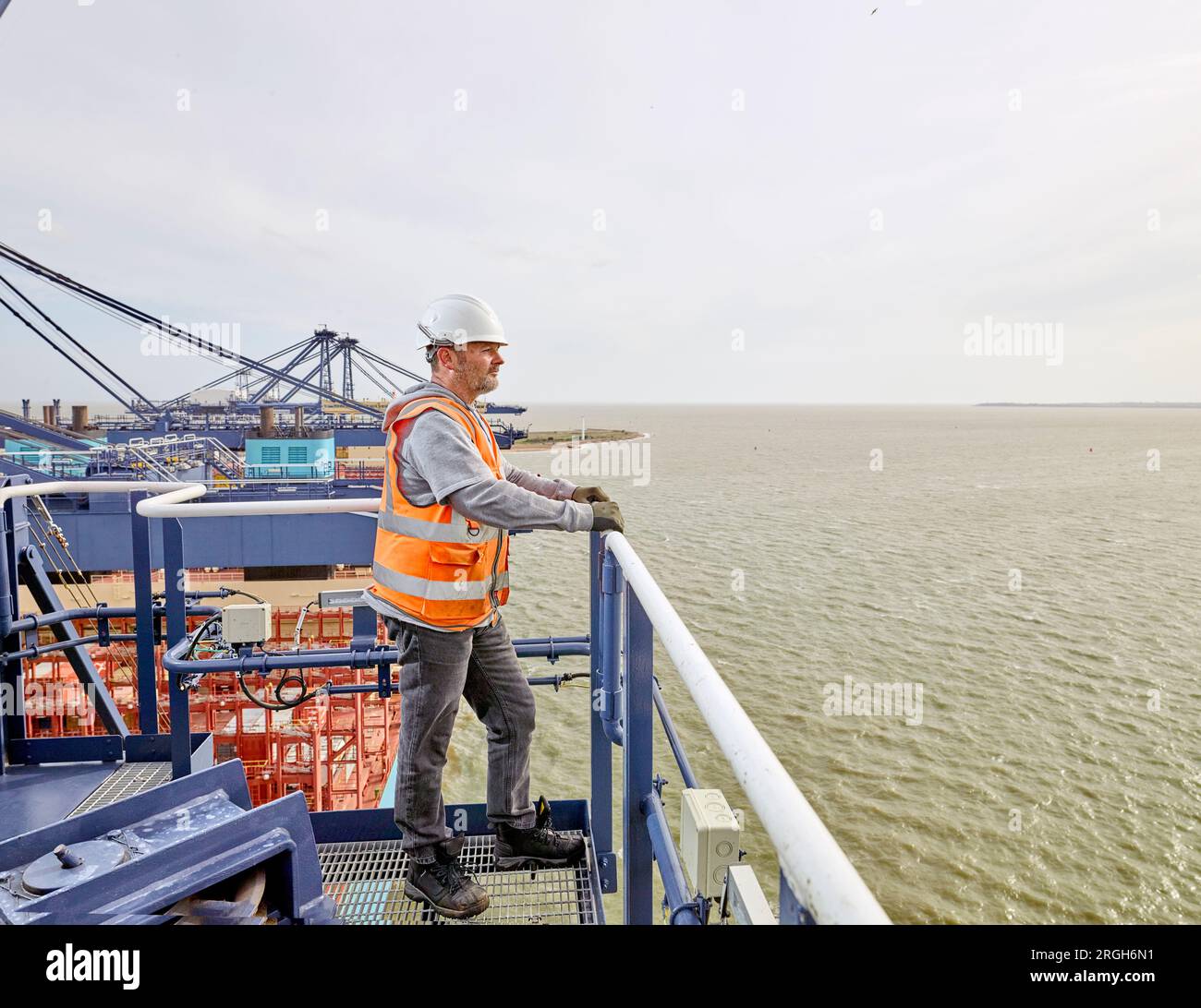 Dock worker looking at view from crane railing Stock Photo - Alamy