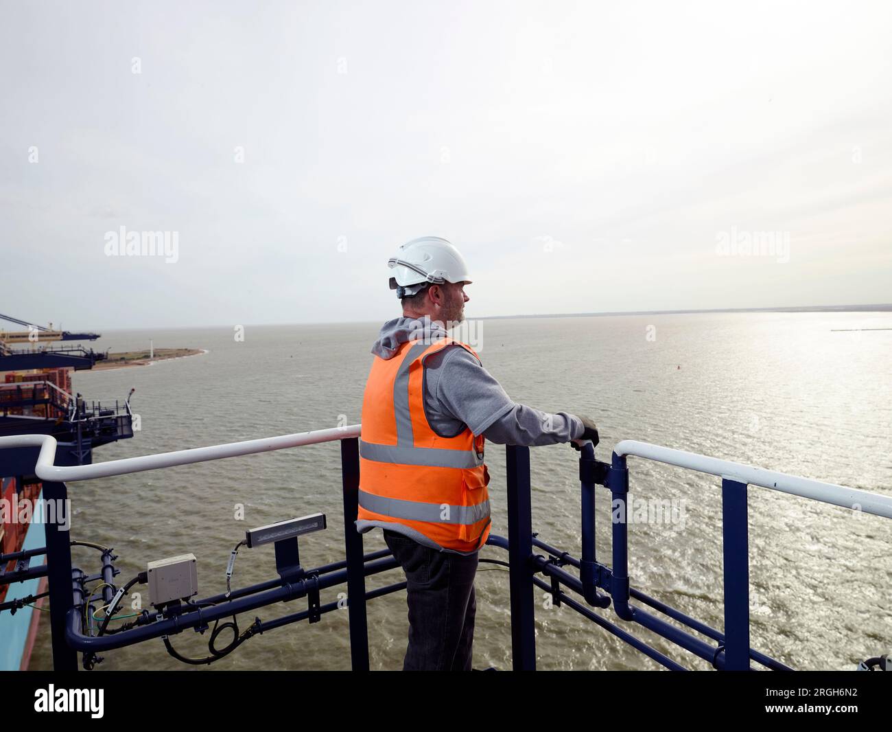 Dock worker looking at view from crane railing Stock Photo - Alamy