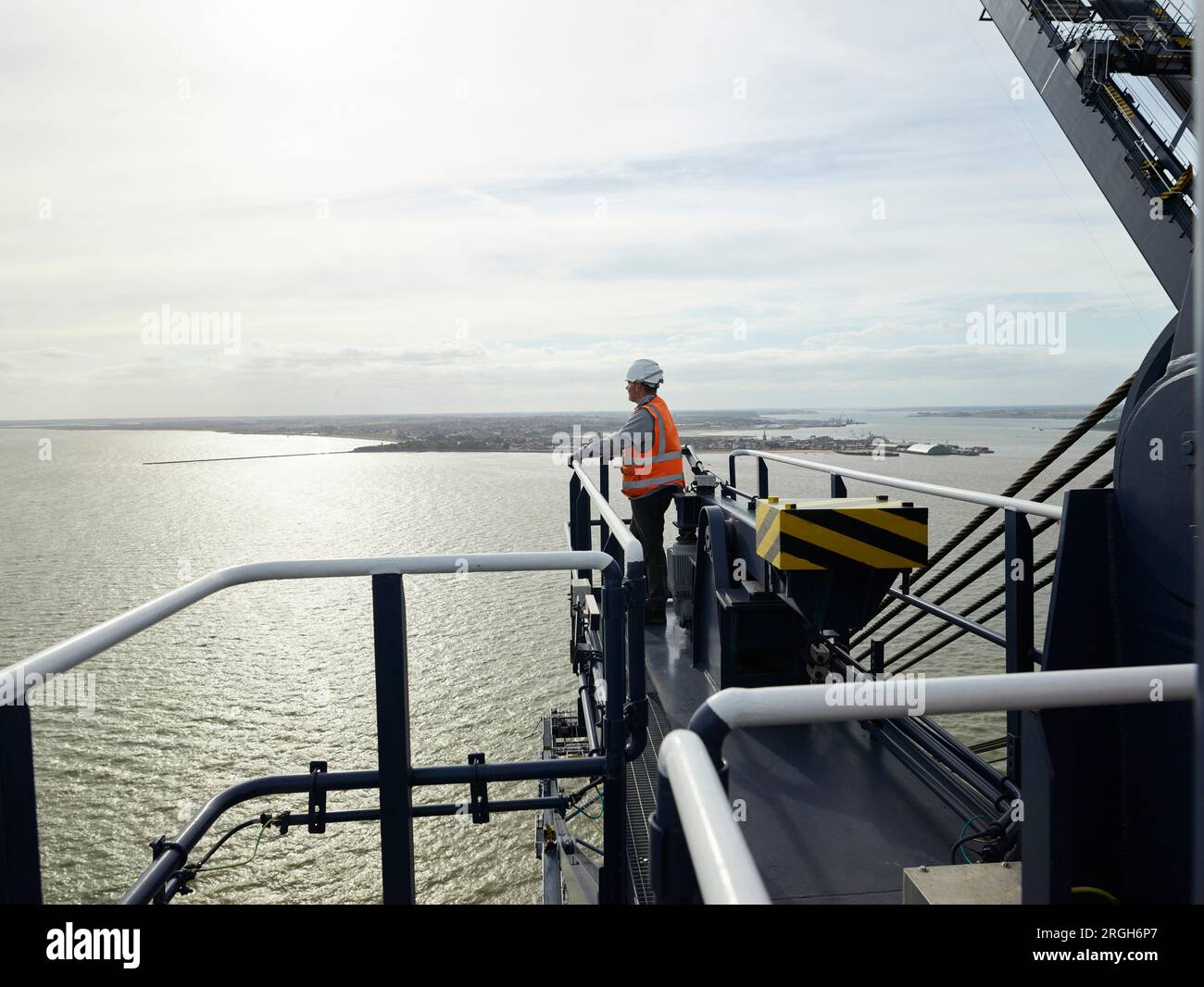 Dock worker looking at view from crane railing Stock Photo - Alamy