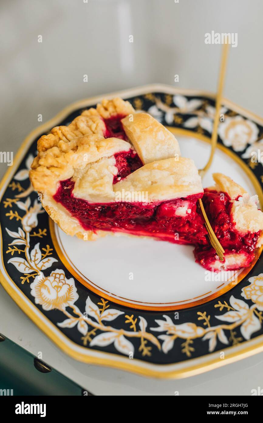 cutting into raspberry pie slice with lattice crust on floral black ...