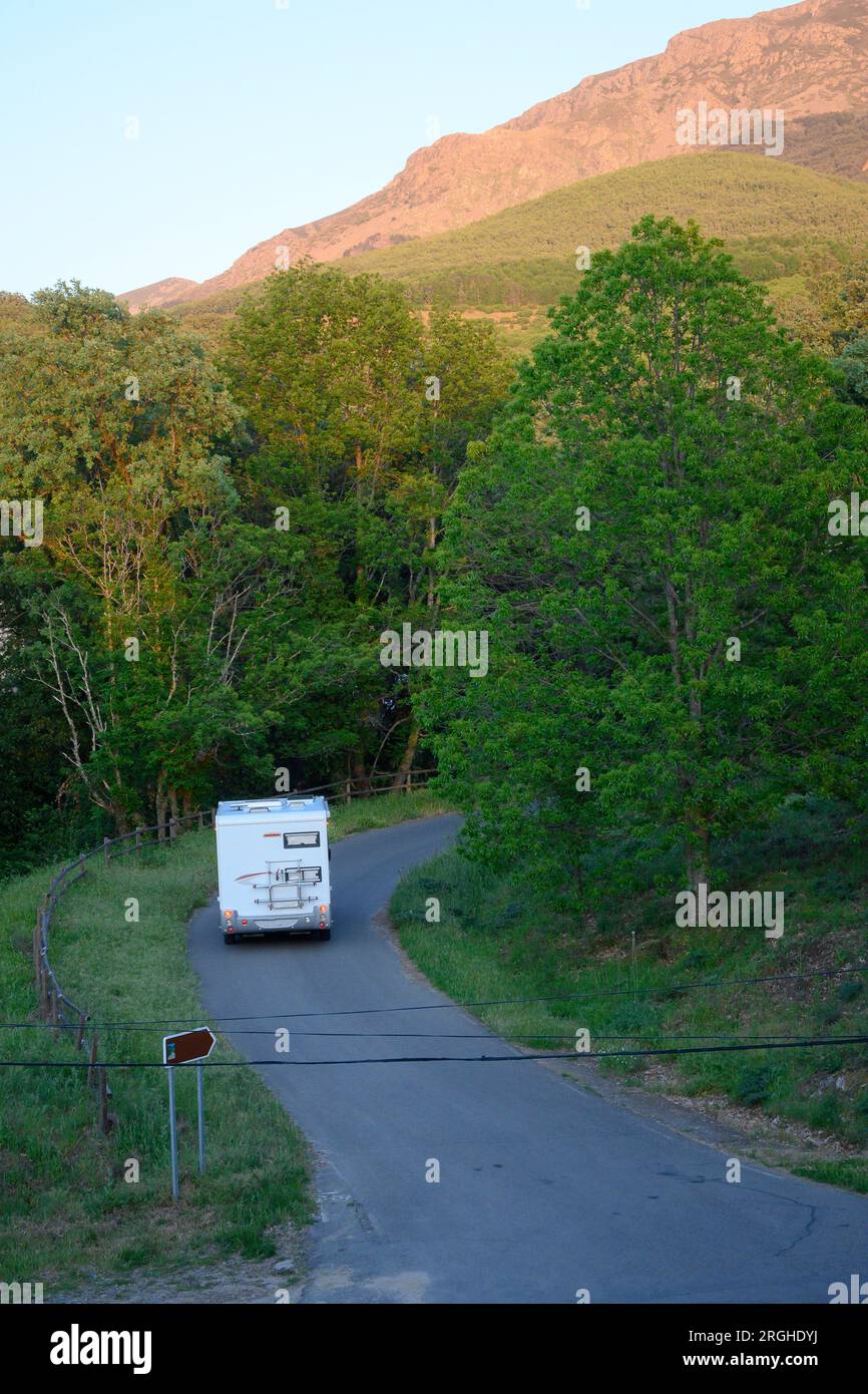 Camper van going up mountain road with green forest and high mountains ...