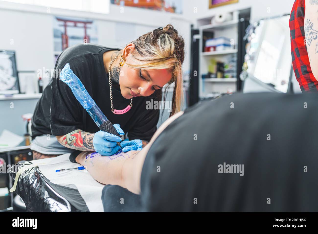 Adult professional female tattoo artist tattooing young woman's leg ...