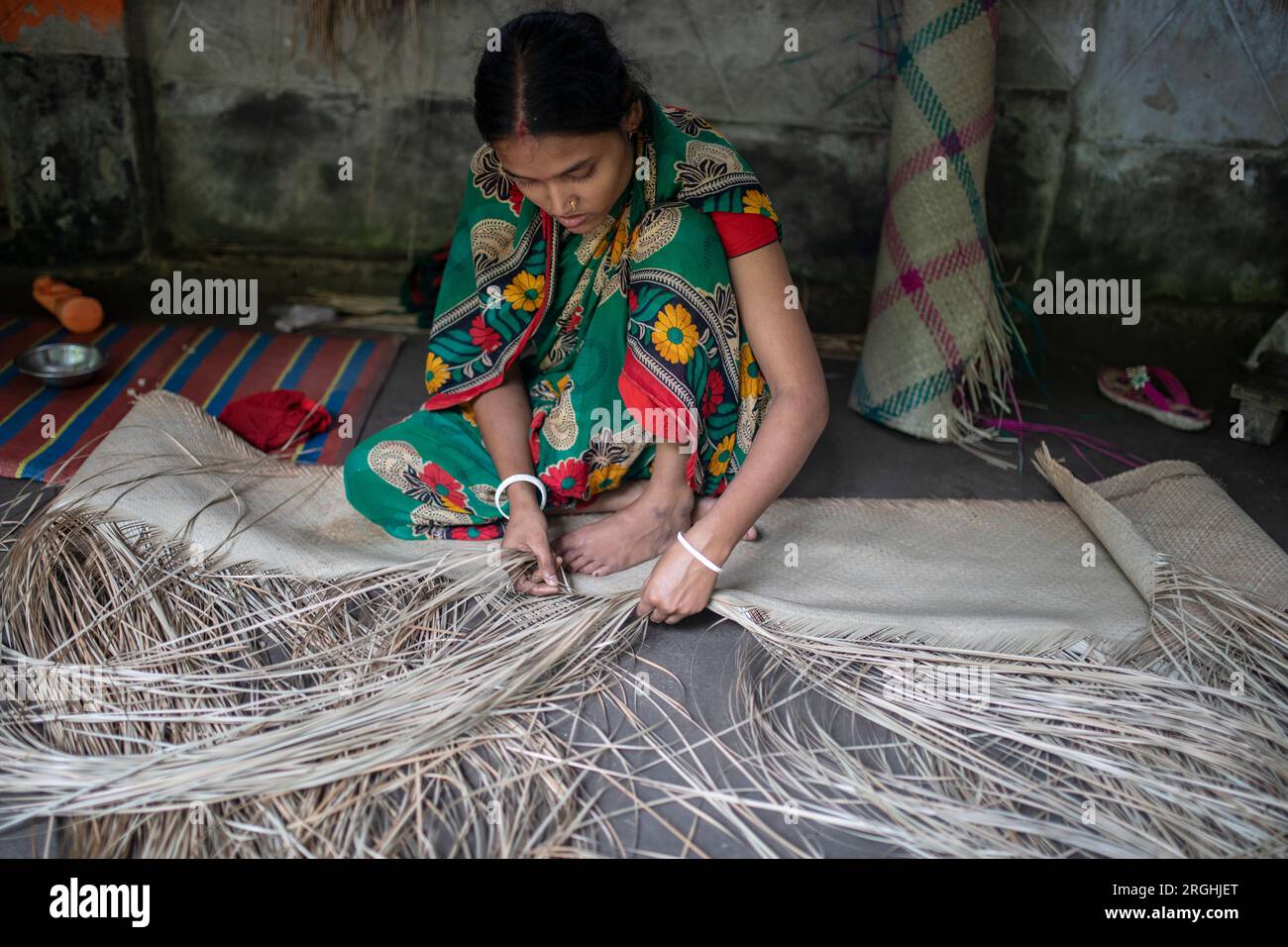 A woman weaves traditional shitol pati (cool mat) at her home in ...