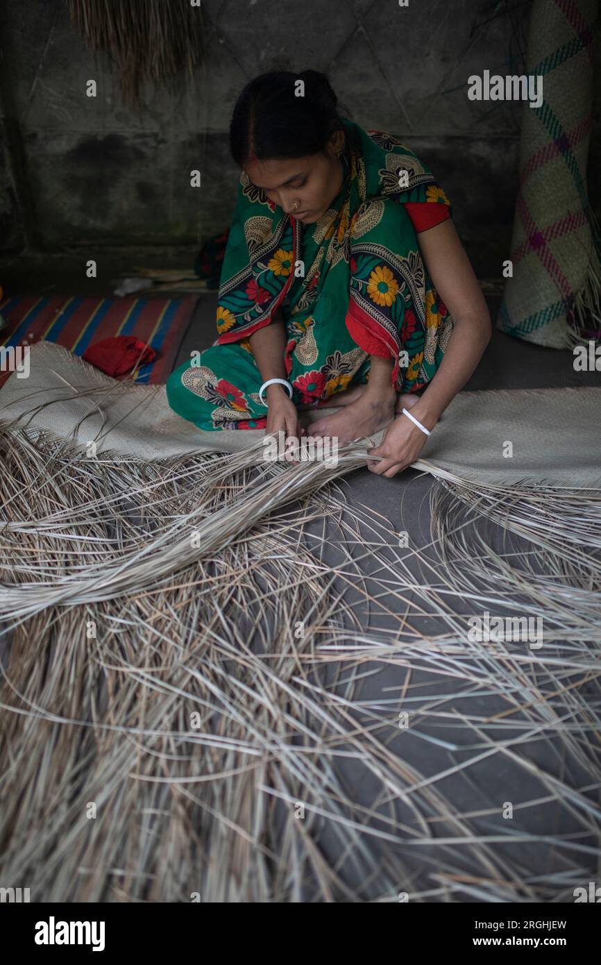 A woman weaves traditional shitol pati (cool mat) at her home in ...