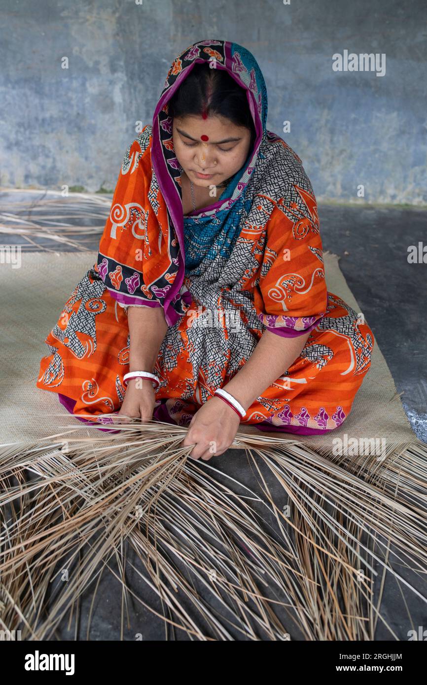A woman weaves traditional shitol pati (cool mat) at her home in ...