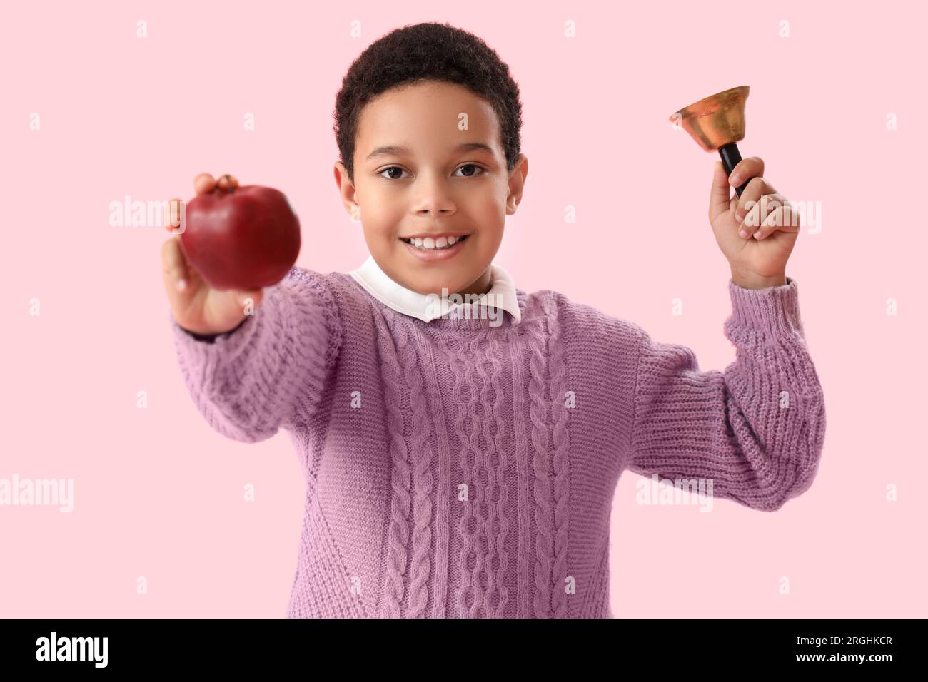Little African-American schoolboy with bell and apple on pink ...
