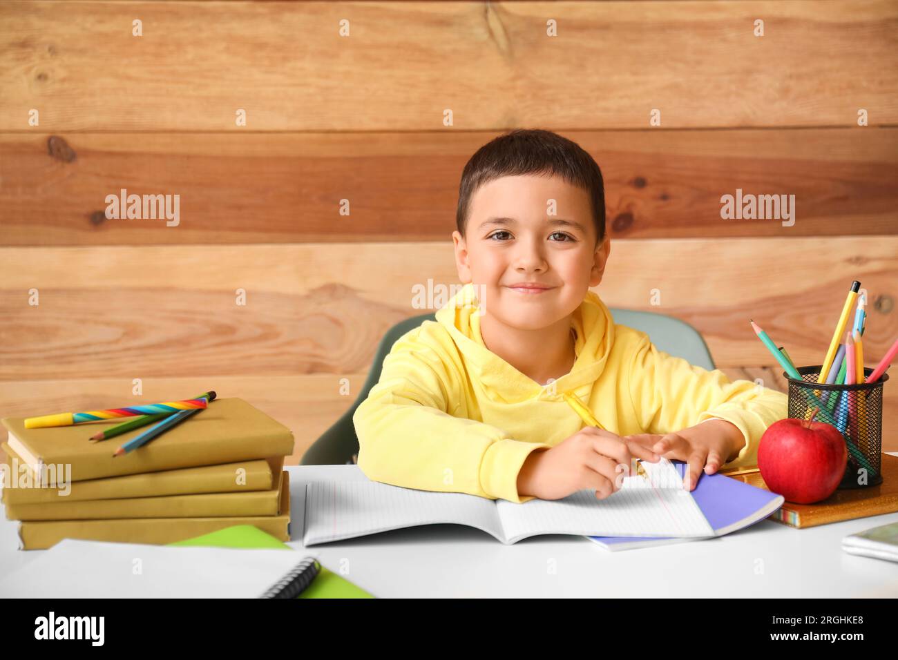 Cute little boy doing homework at table near wooden wall Stock Photo ...