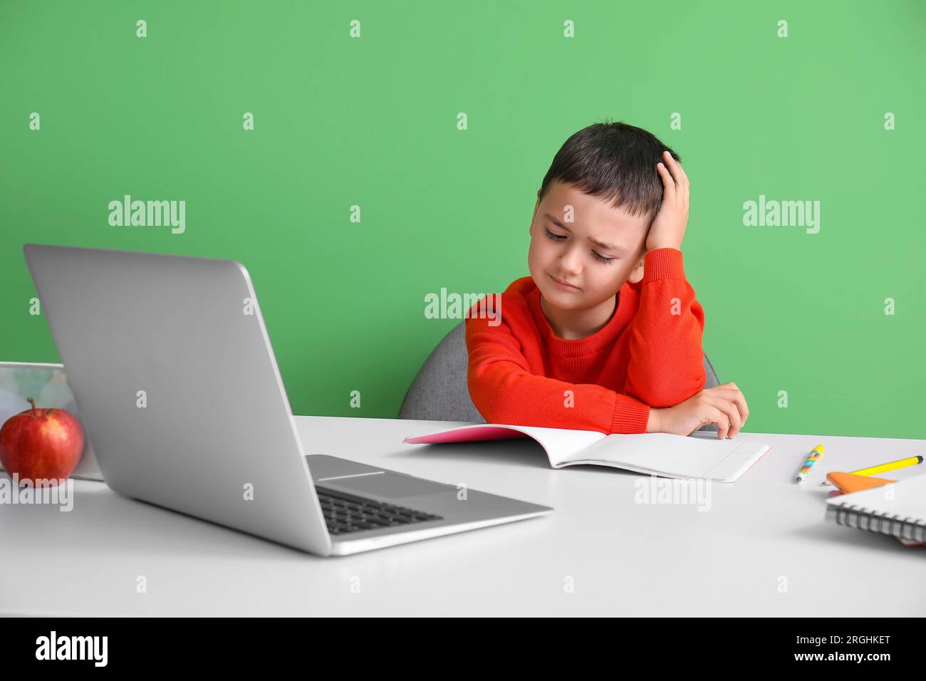 Stressed little boy doing homework at table near green wall Stock Photo ...