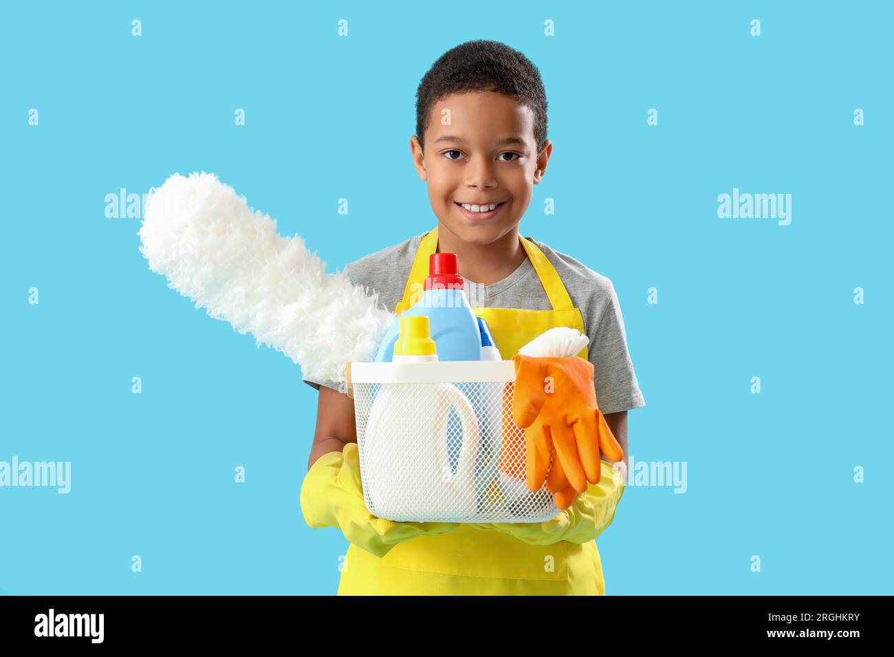 Little African-American boy with cleaning supplies in basket on blue ...