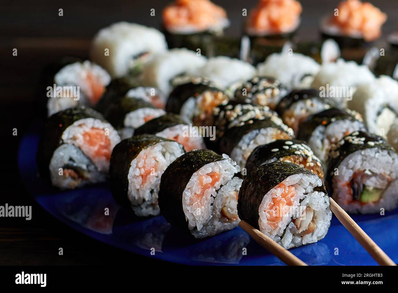 Beautiful female hands take sushi with chopsticks. Dark background. Wooden plank. Side view ...
