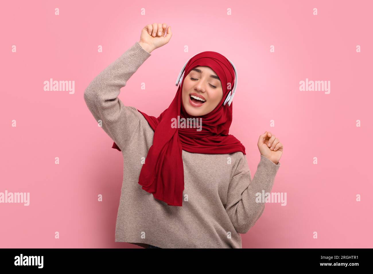 Muslim woman in hijab and headphones dancing on pink background Stock ...