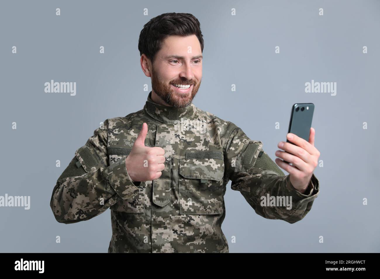 Happy soldier using video chat on smartphone and showing thumb up ...