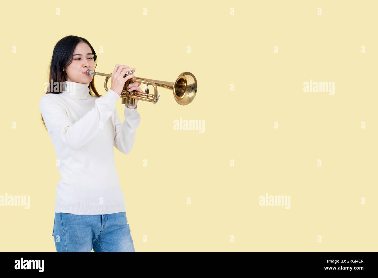 A pretty and talented Asian woman is playing the trumpet while standing ...