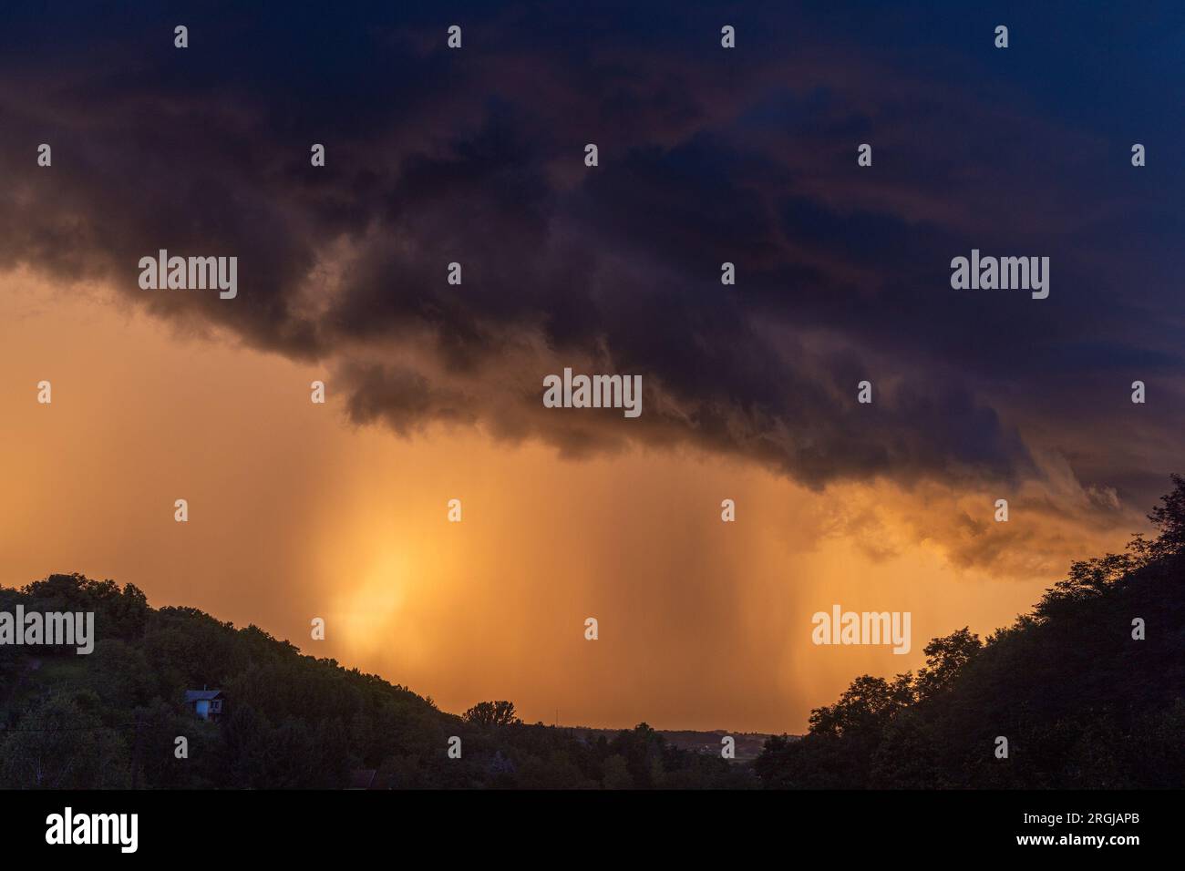 Dramatic storm clouds with an intense rain lit by the setting sun ...
