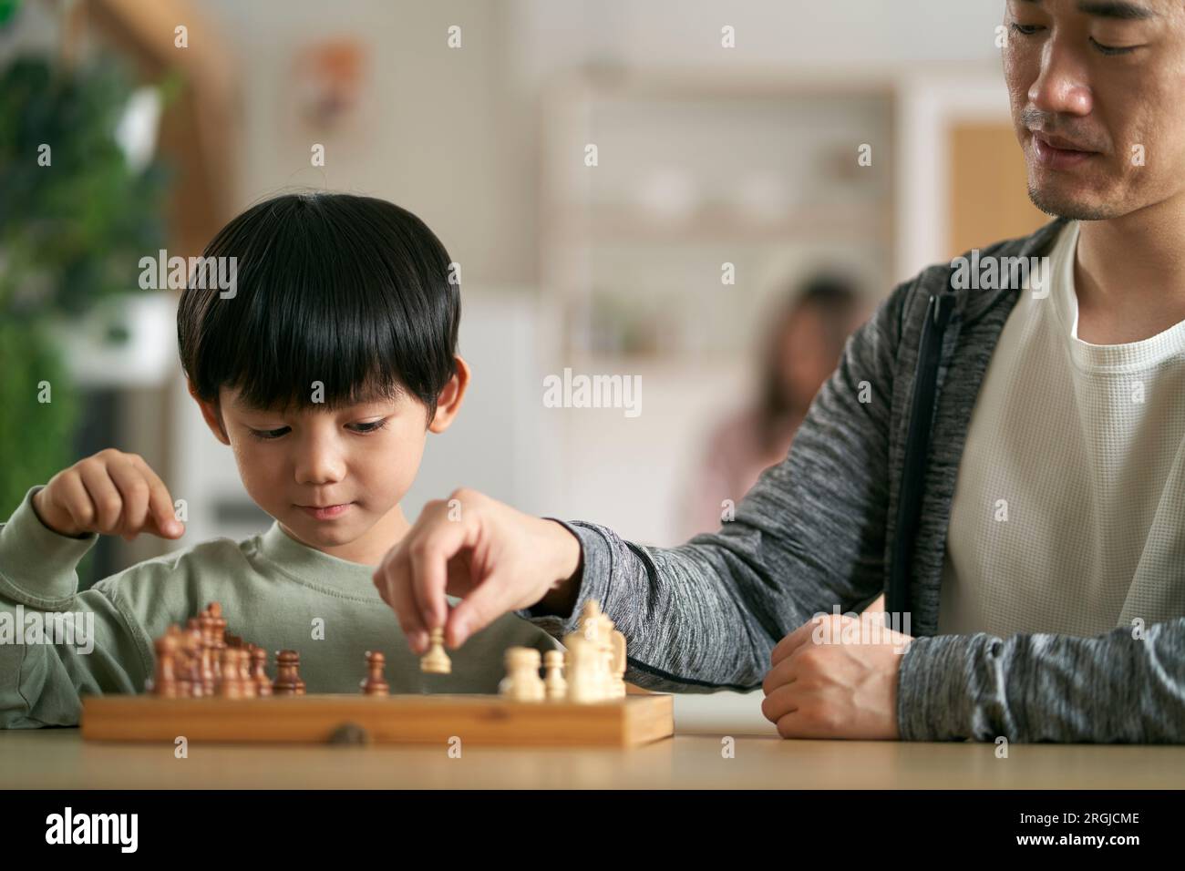 asian father and son sitting at kitchen table at home playing chess ...