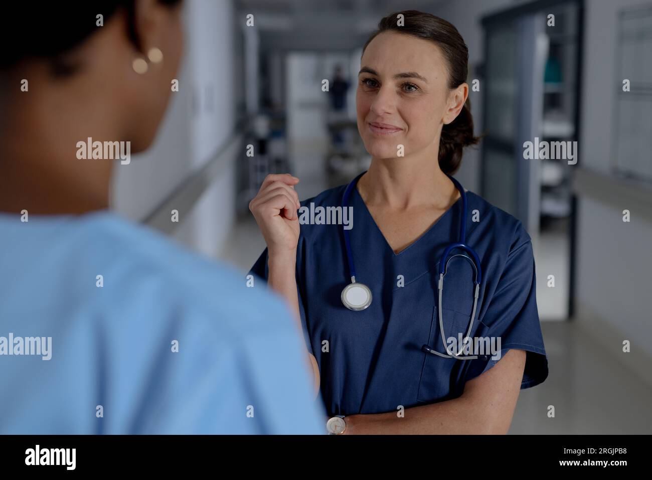 Diverse female doctors wearing scrubs discussing work in corridor at ...
