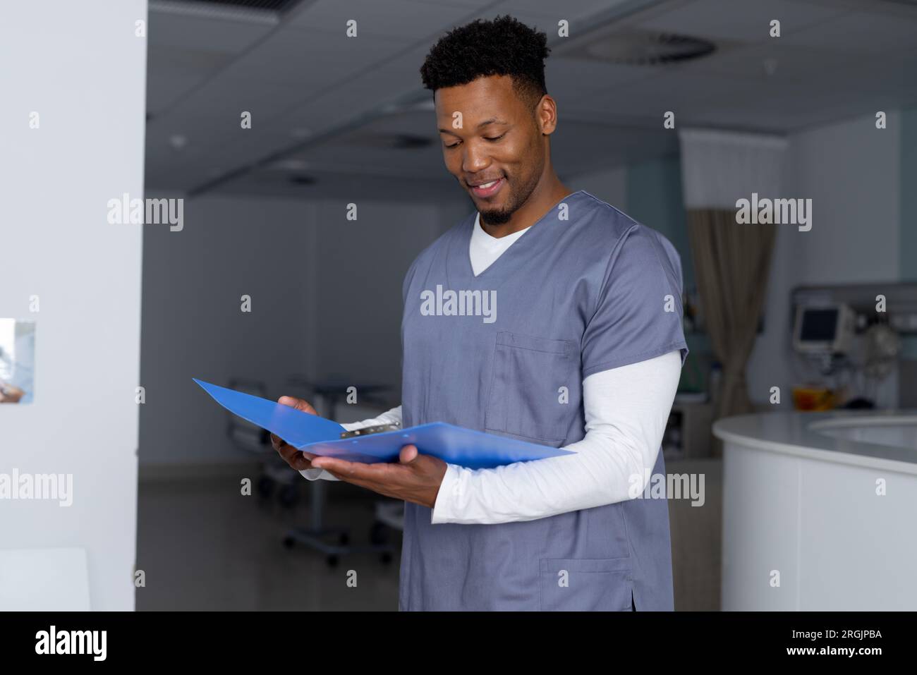 Happy african american male doctor wearing scrubs holding documents in ...
