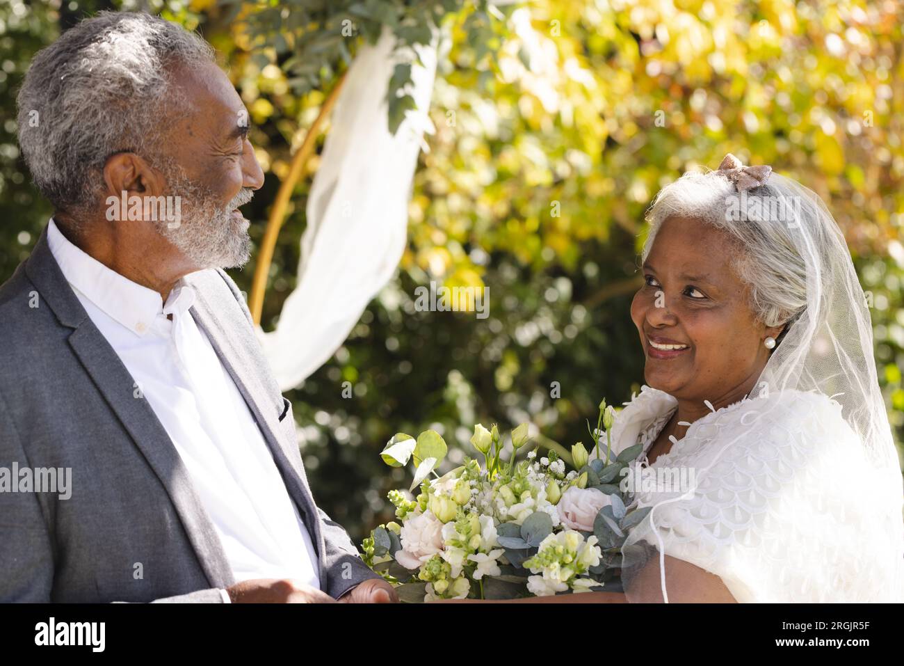 Happy senior biracial bride and groom during wedding ceremony in sunny ...