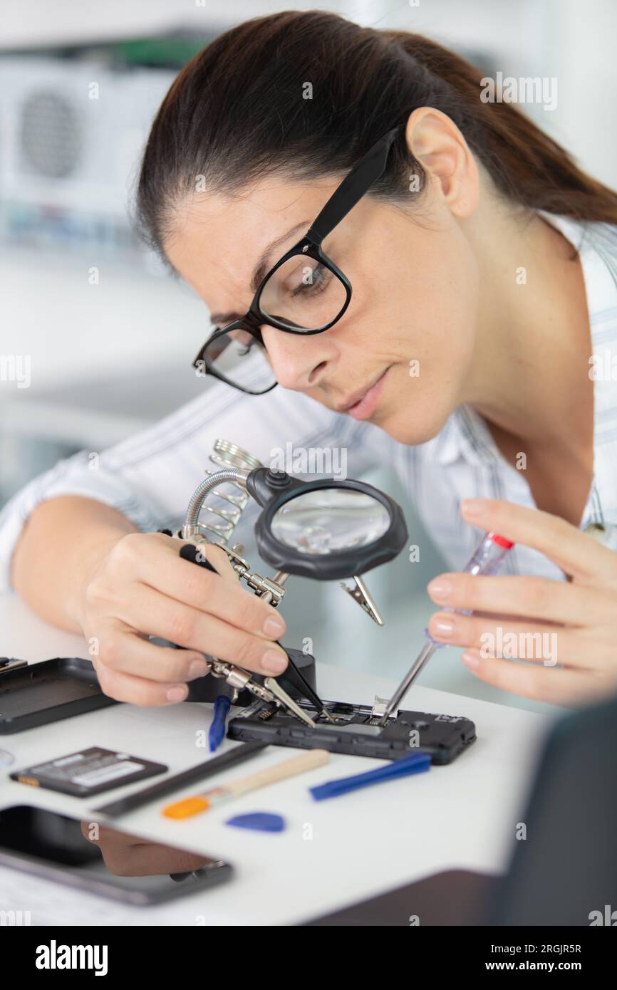 woman repairs a mobile phone looking through a magnifying glass Stock ...