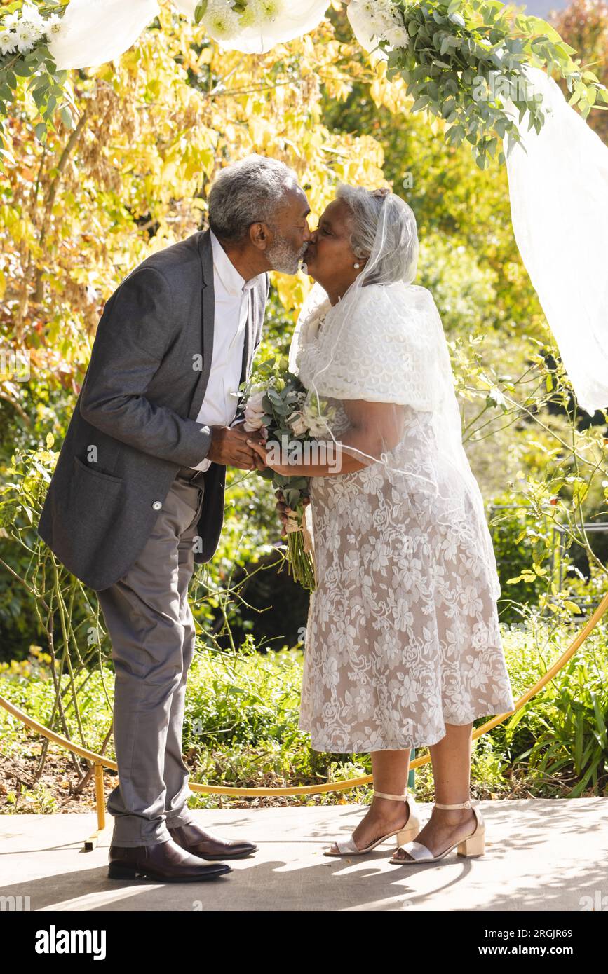 Happy senior biracial bride and groom kissing at wedding ceremony in ...