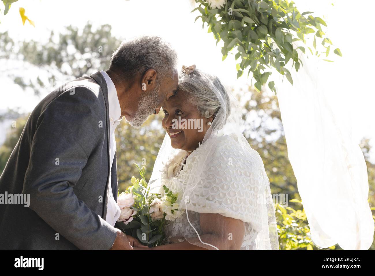 Happy senior biracial bride and groom holding hands at sunny outdoor ...
