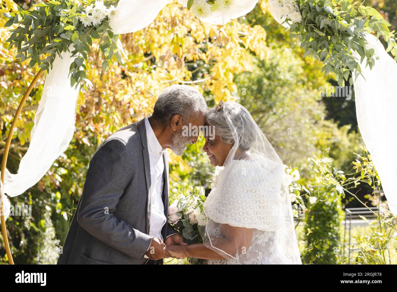 Happy senior biracial bride and groom during wedding ceremony in sunny ...