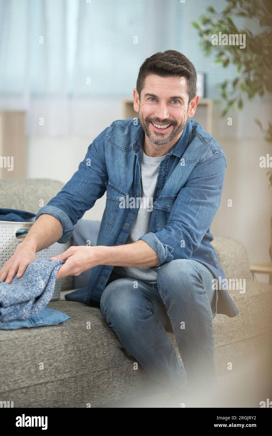 full length of young man folding laundry on a sofa Stock Photo - Alamy