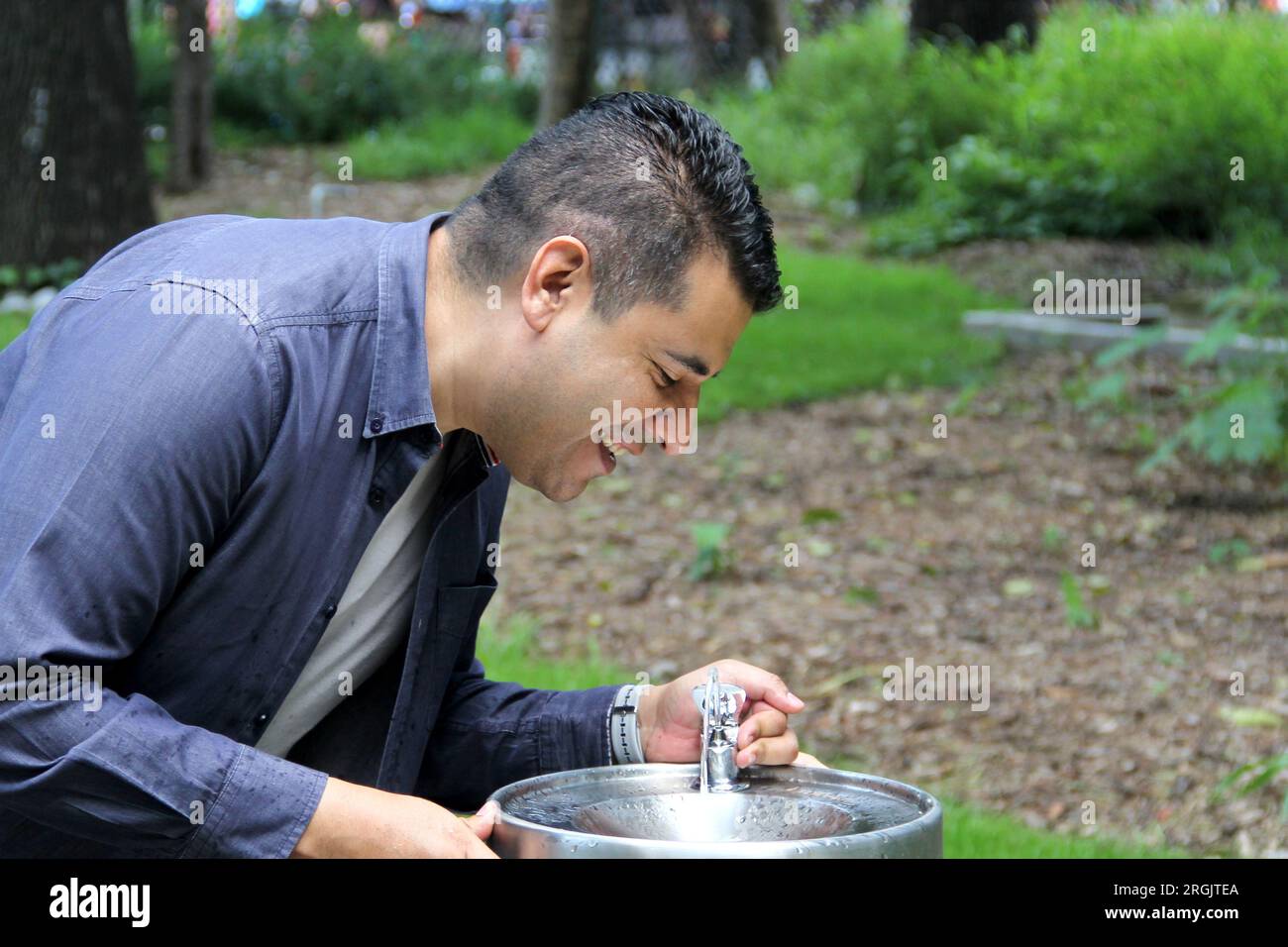 Dark-haired 40-year-old Latino man drinks drinking water from a public ...