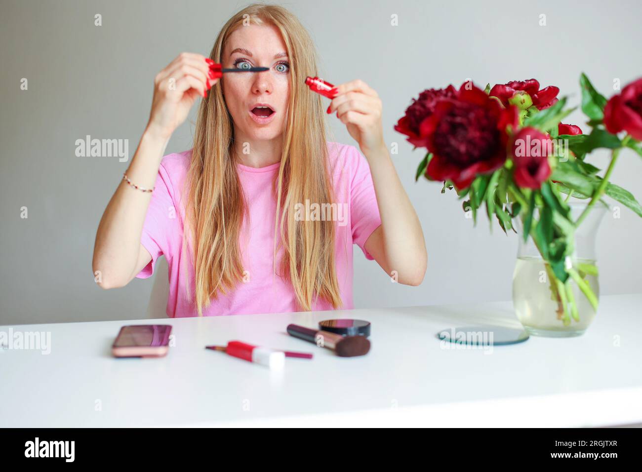 Beautiful young woman putting lash mascara on eyelashes scared in shock ...